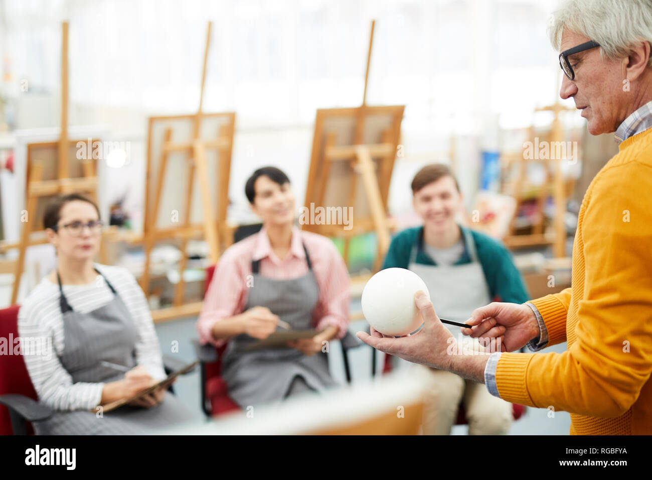 Side view portrait of mature art teacher holding sphere and explaining ...