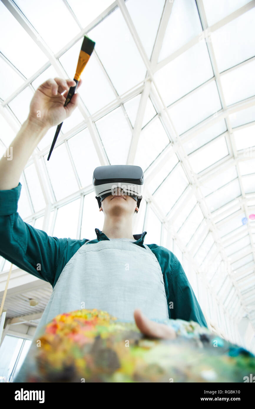 Low angle portrait of young man wearing VR headset painting picture on ...