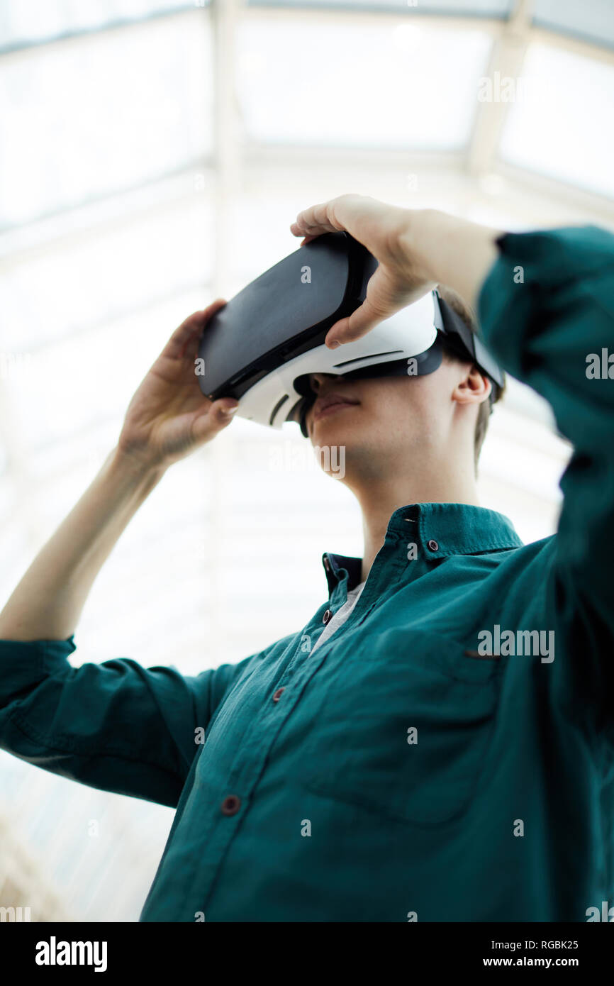 Low angle portrait of young man wearing VR headset standing under ...