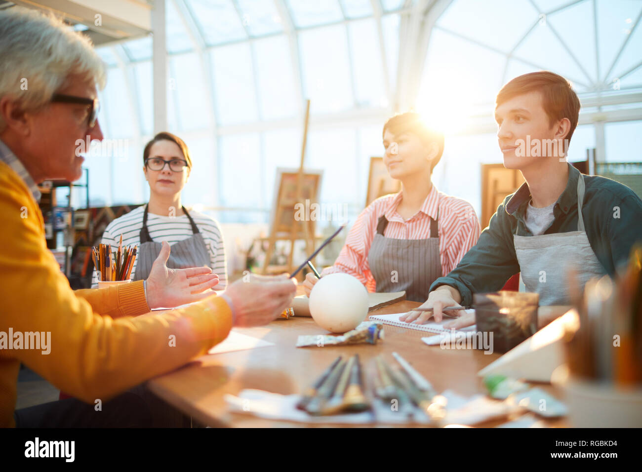 Portrait of group of students listening to senior art teacher during ...