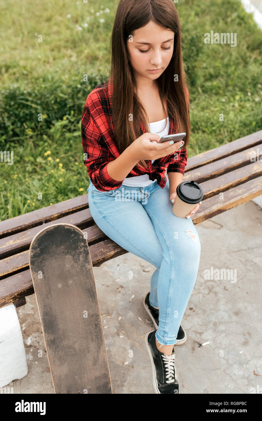 Summer teenager girl sitting on a bench, holding a smartphone in her ...