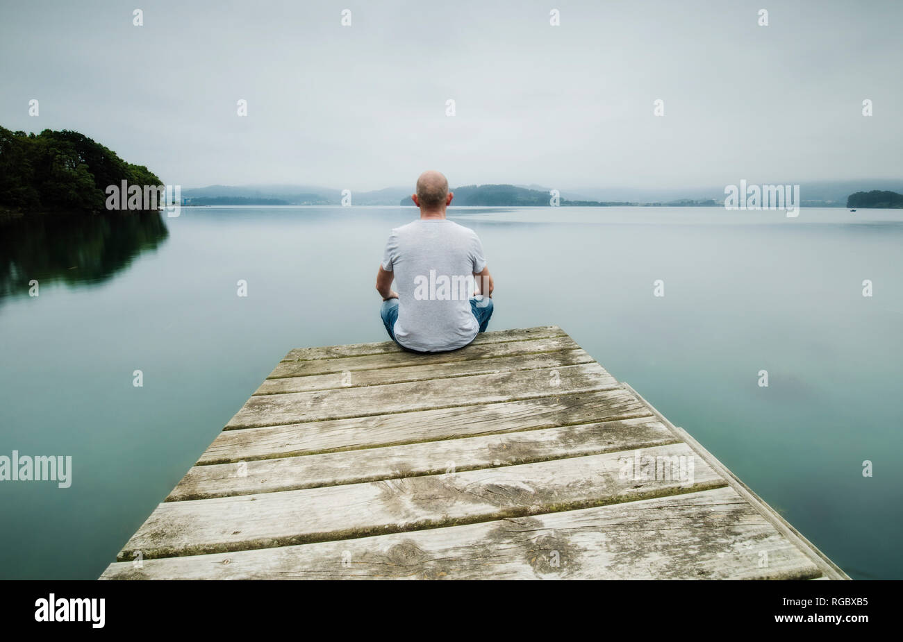Back view of man sitting on jetty looking at distance Stock Photo - Alamy