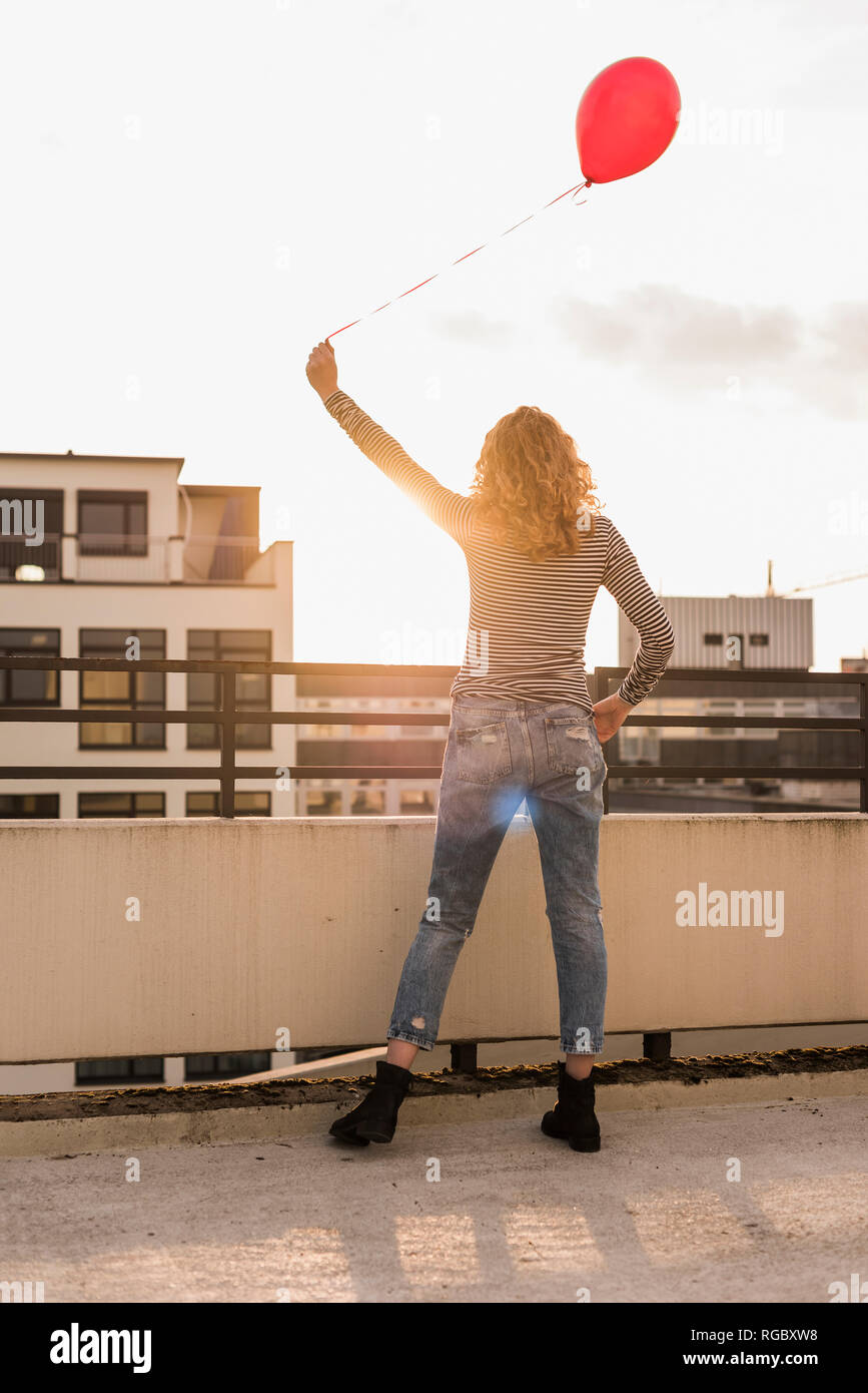 Back view of young young with red balloon standing on roof terrace at ...