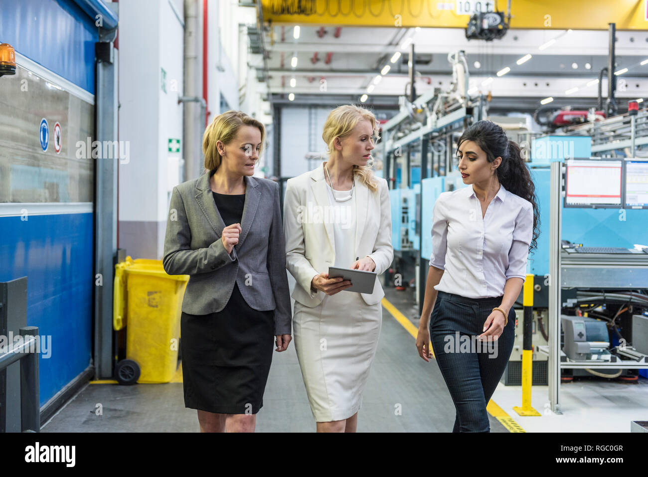 Three women with tablet walking and talking in factory shop floor Stock ...