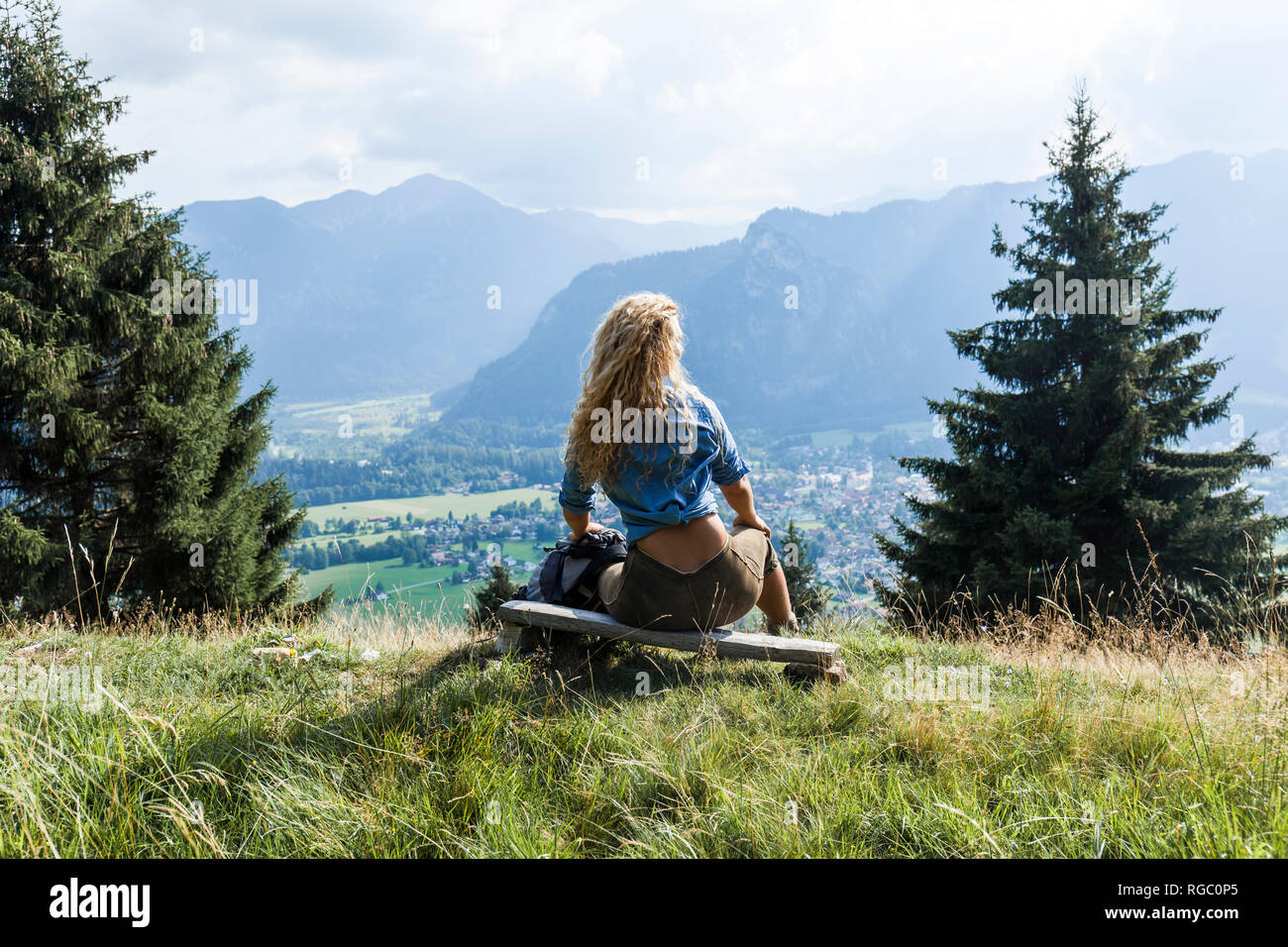 Germany, Bavaria, Oberammergau, young woman hiking sitting on bench on ...
