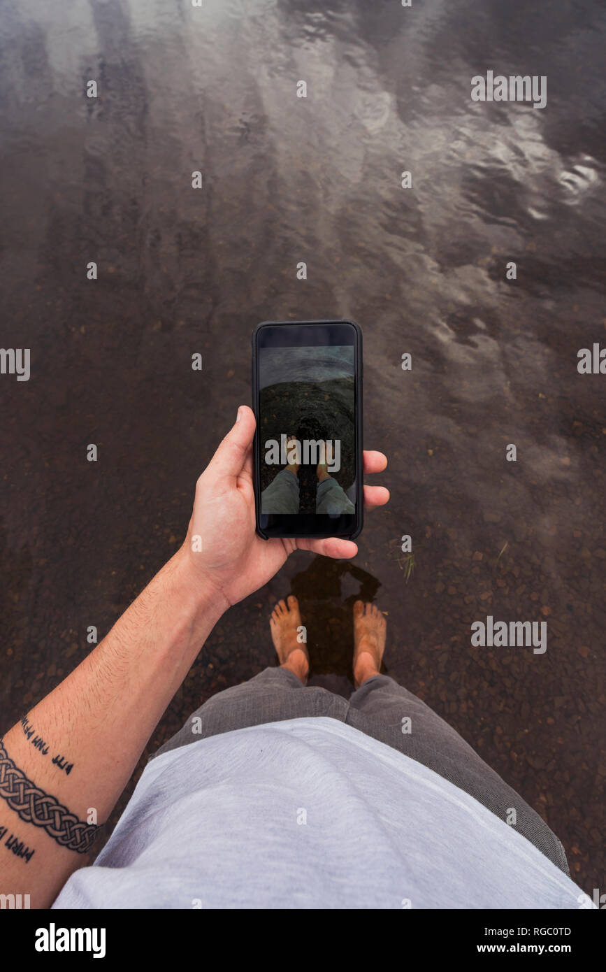 Man taking a cell phone picture with feet in water of a lake Stock ...