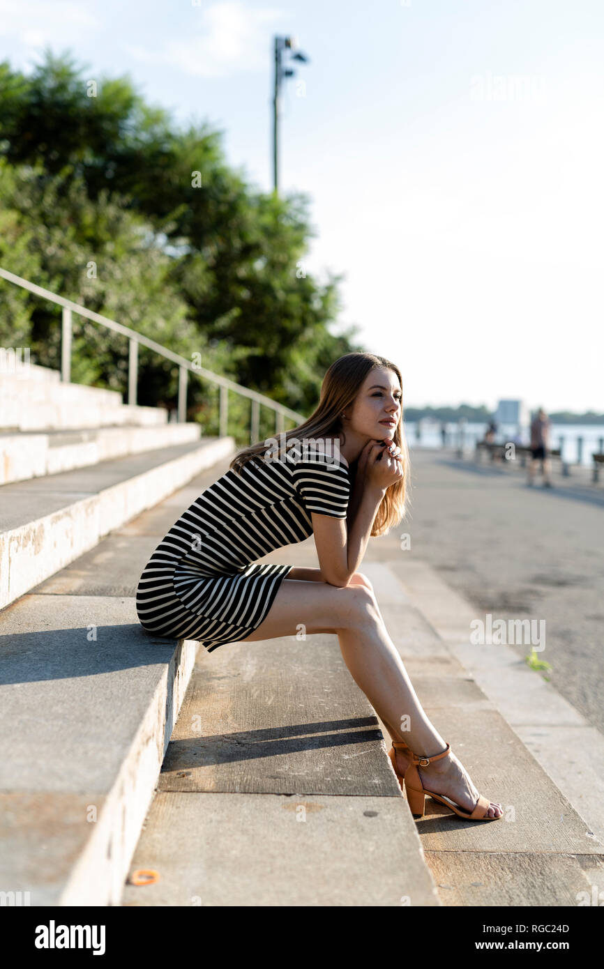 USA, New York, Brooklyn, young woman relaxing on stairs enjoying sunset ...