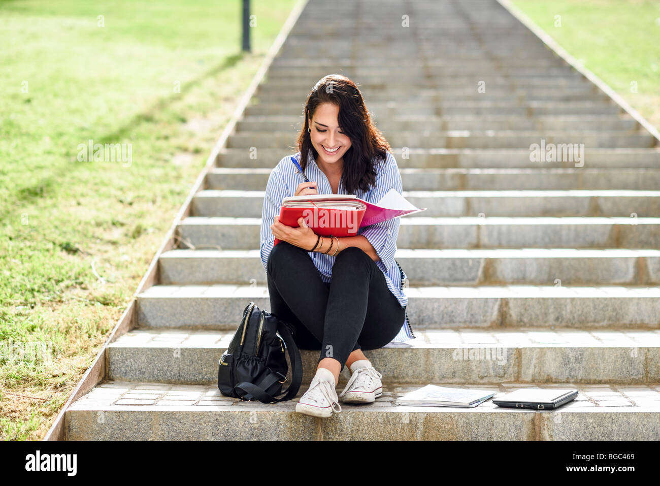 Smiling student sitting stairs outdoors taking notes notebook hi-res ...