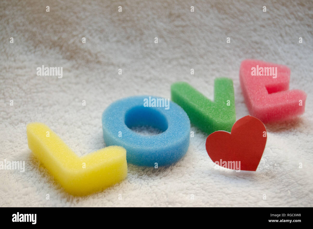 Sponge letters creating word love and red paper heart over white soft ...