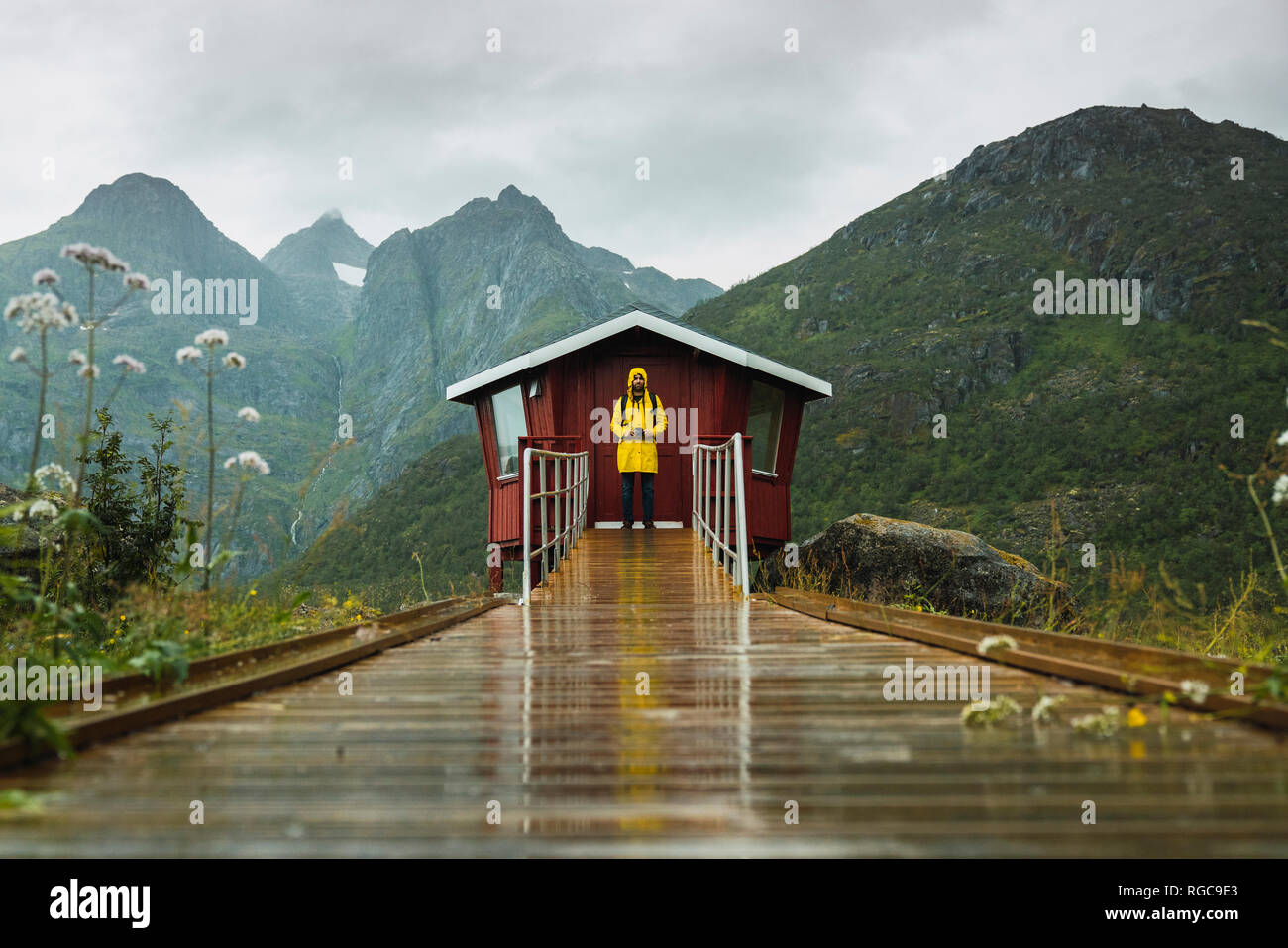 Man in yellow rain jacket waiting at red wood shack, Lapland, Norway ...