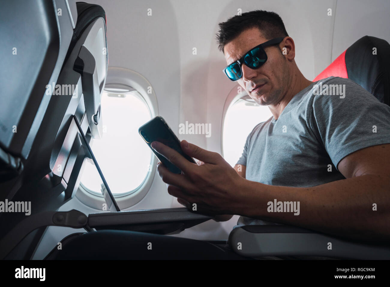 Man in airplane, using smartphone, headphones Stock Photo - Alamy
