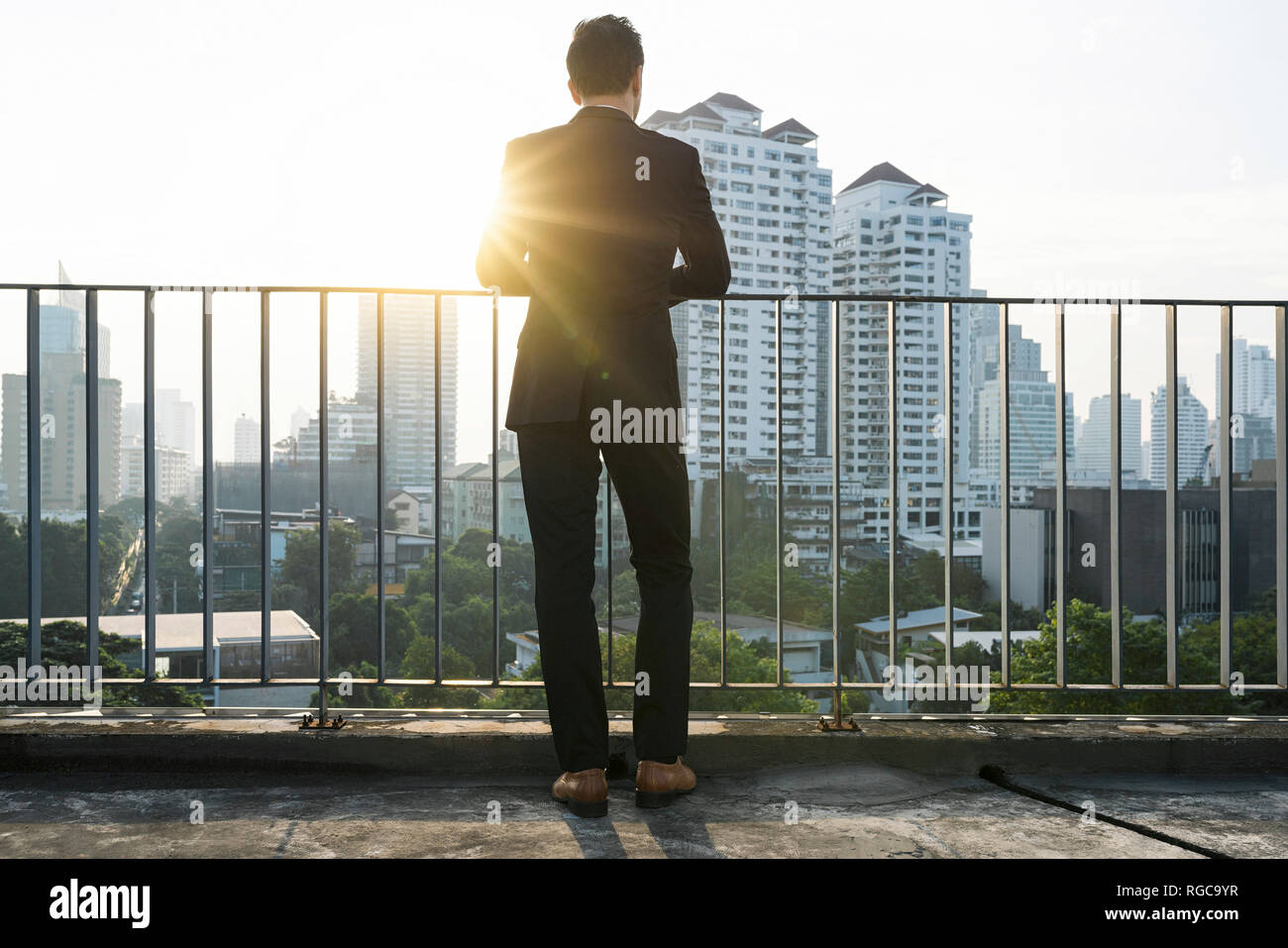 Business man in suit leaning on handrail in sunset on city rooftop ...