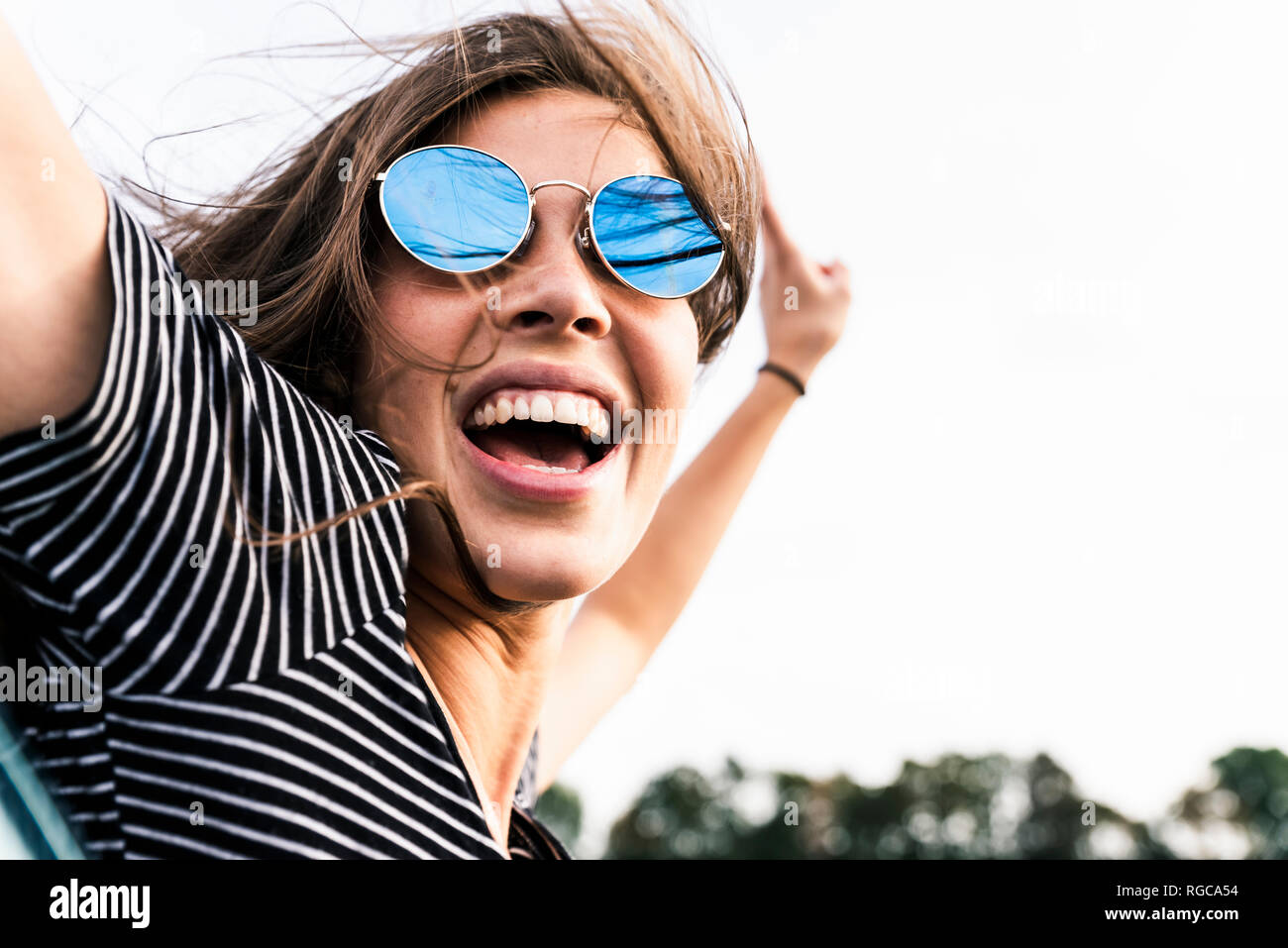 Carefree young woman leaning out of car window screaming Stock Photo ...