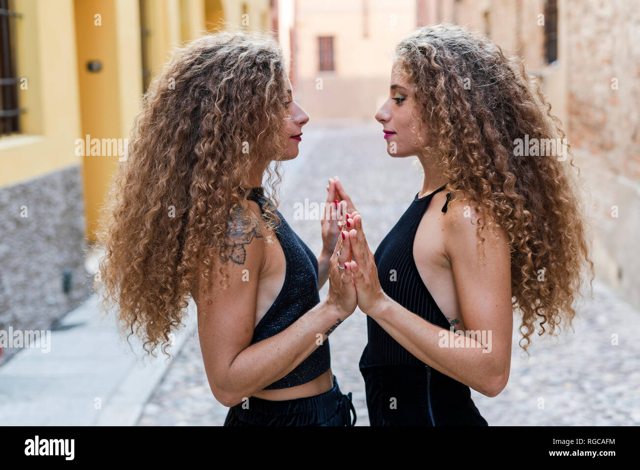 Side view of twin sisters standing face to face touching hands Stock ...