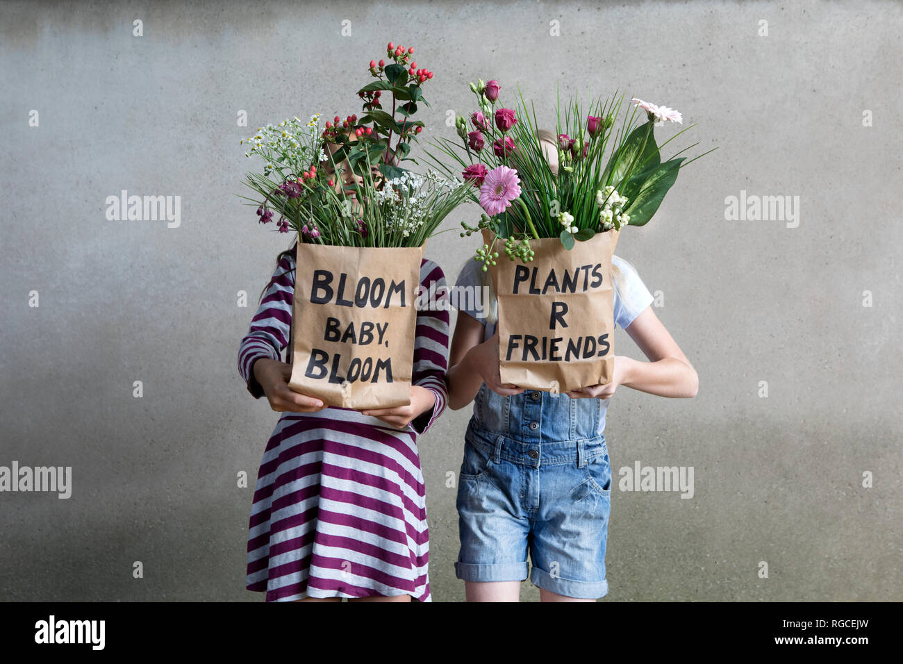 Two girls standing side side hiding behind paper bags flowers hi-res ...