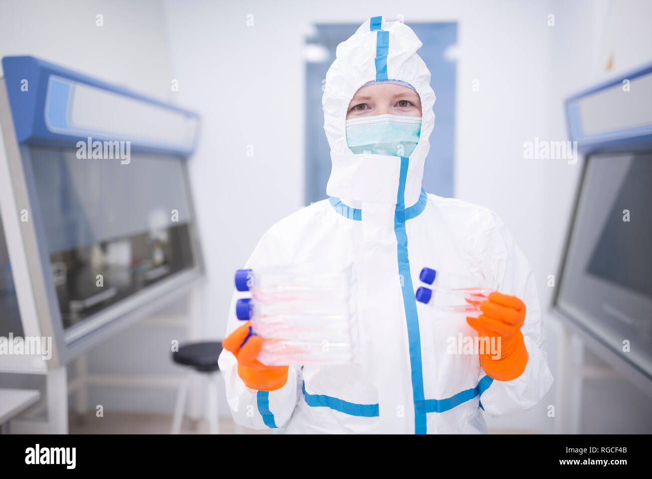 Lab technician wearing cleanroom overall holding cultivation containers ...