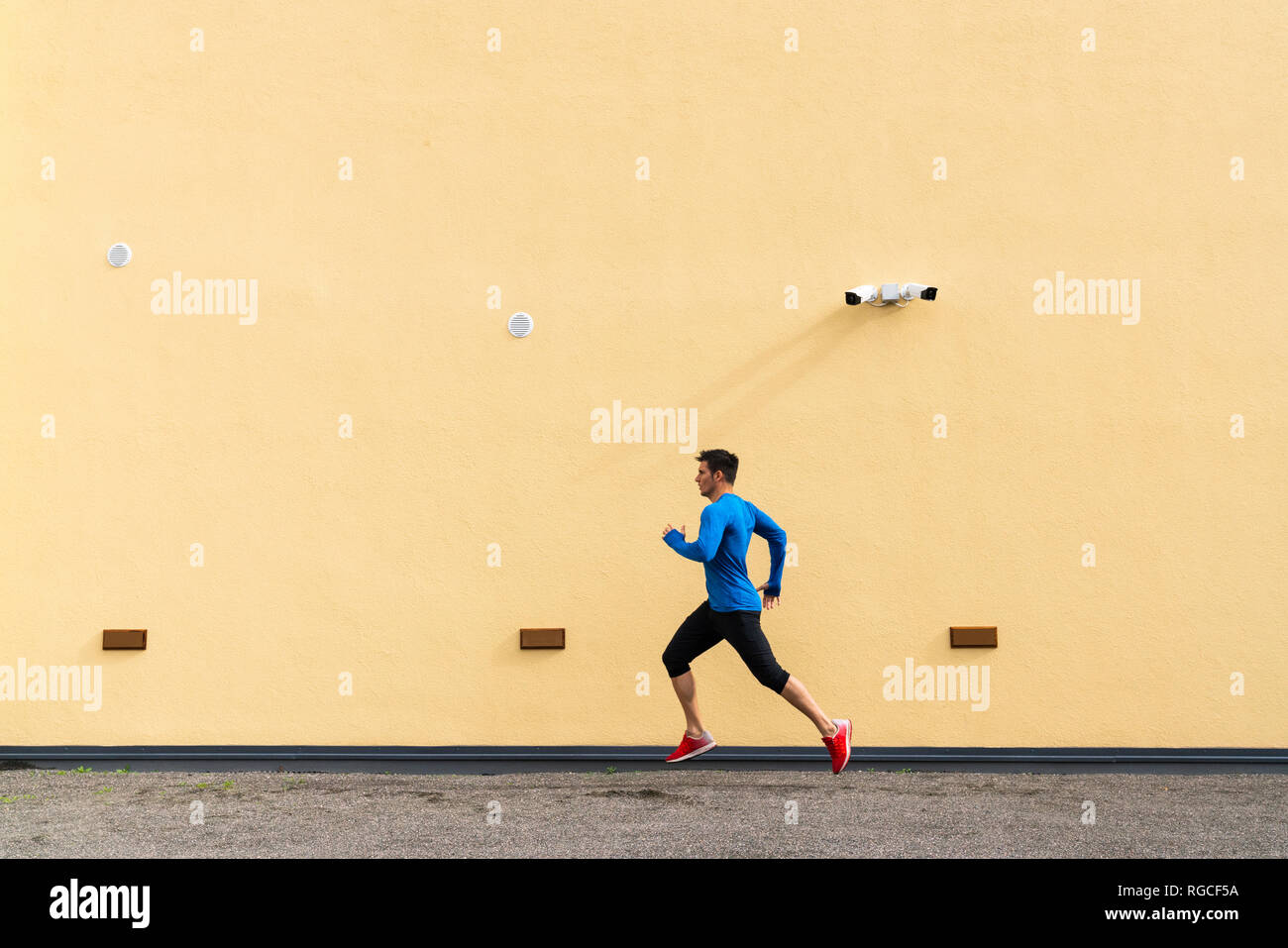 Sportive man running along yellow wall with CCTV camera Stock Photo - Alamy