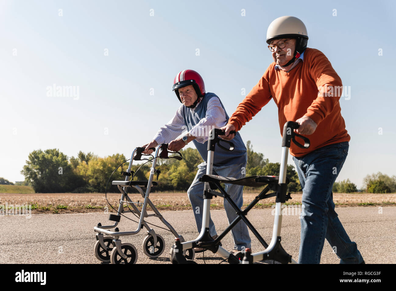 Two old friends wearing safety helmets, competing in a wheeled walker ...