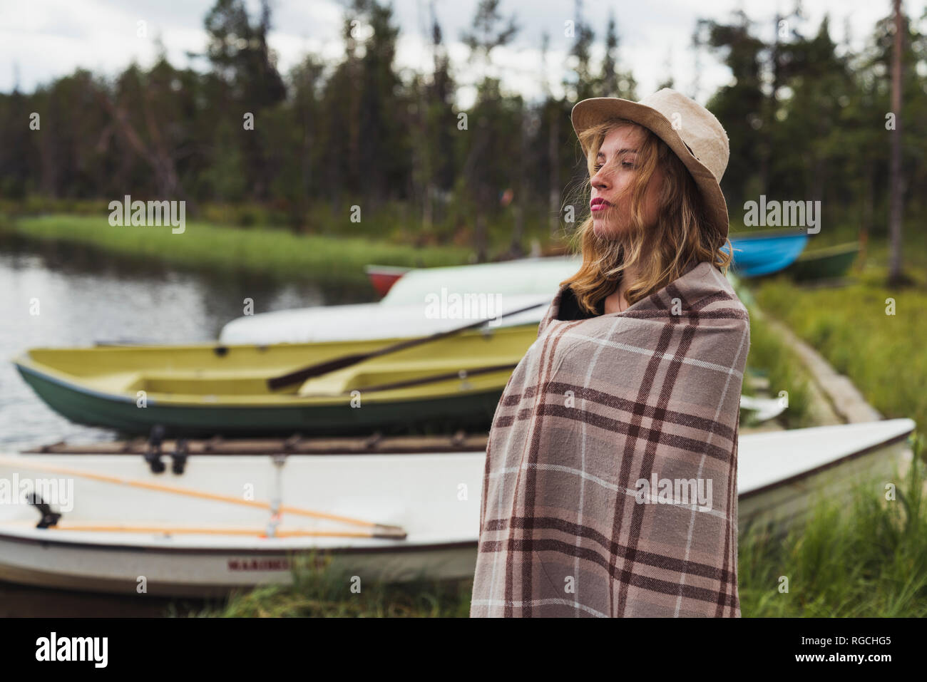 Finland, Lapland, woman wearing a hat wrapped in a blanket standing at ...