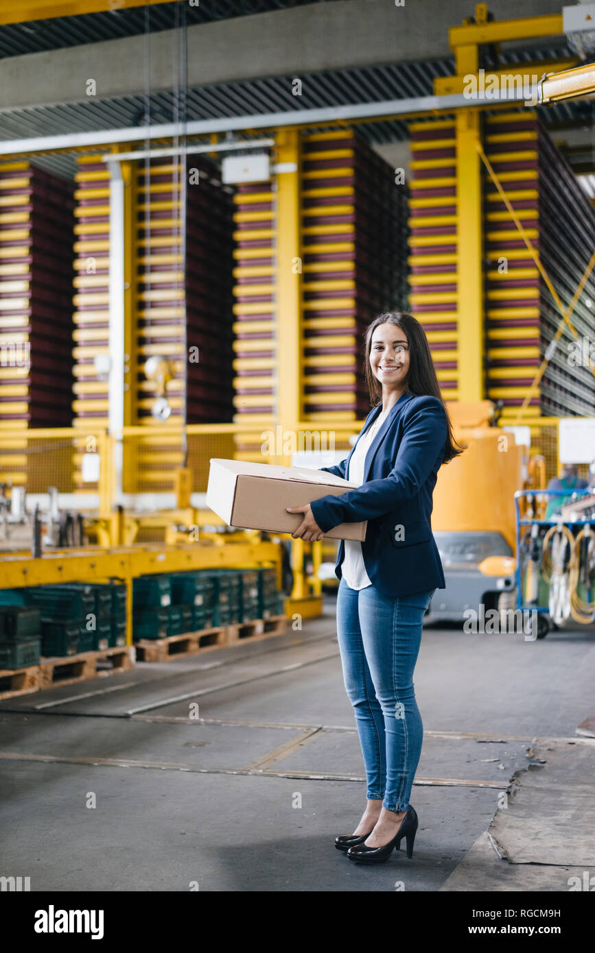 Young woman working at parcel service, carrying parcel in warehouse ...