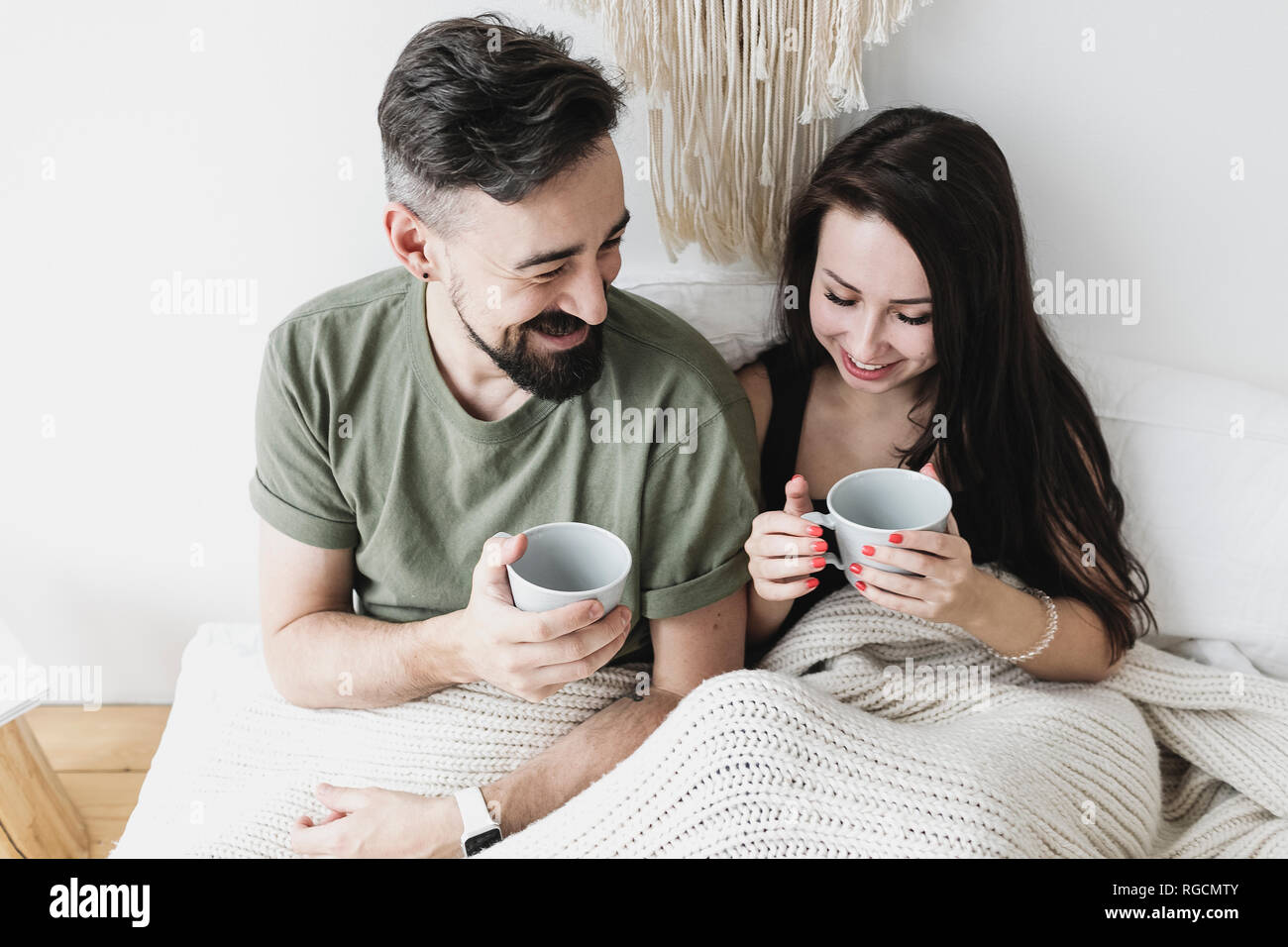 Happy couple sitting in bed, drinking coffee, having fun Stock Photo ...