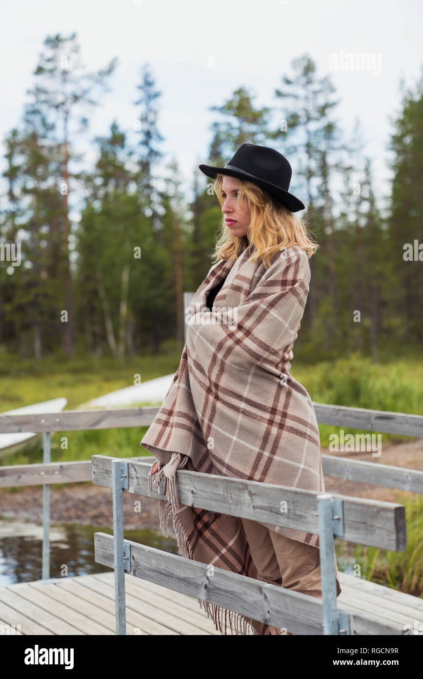 Finland, Lapland, woman wearing a hat wrapped in a blanket standing on ...