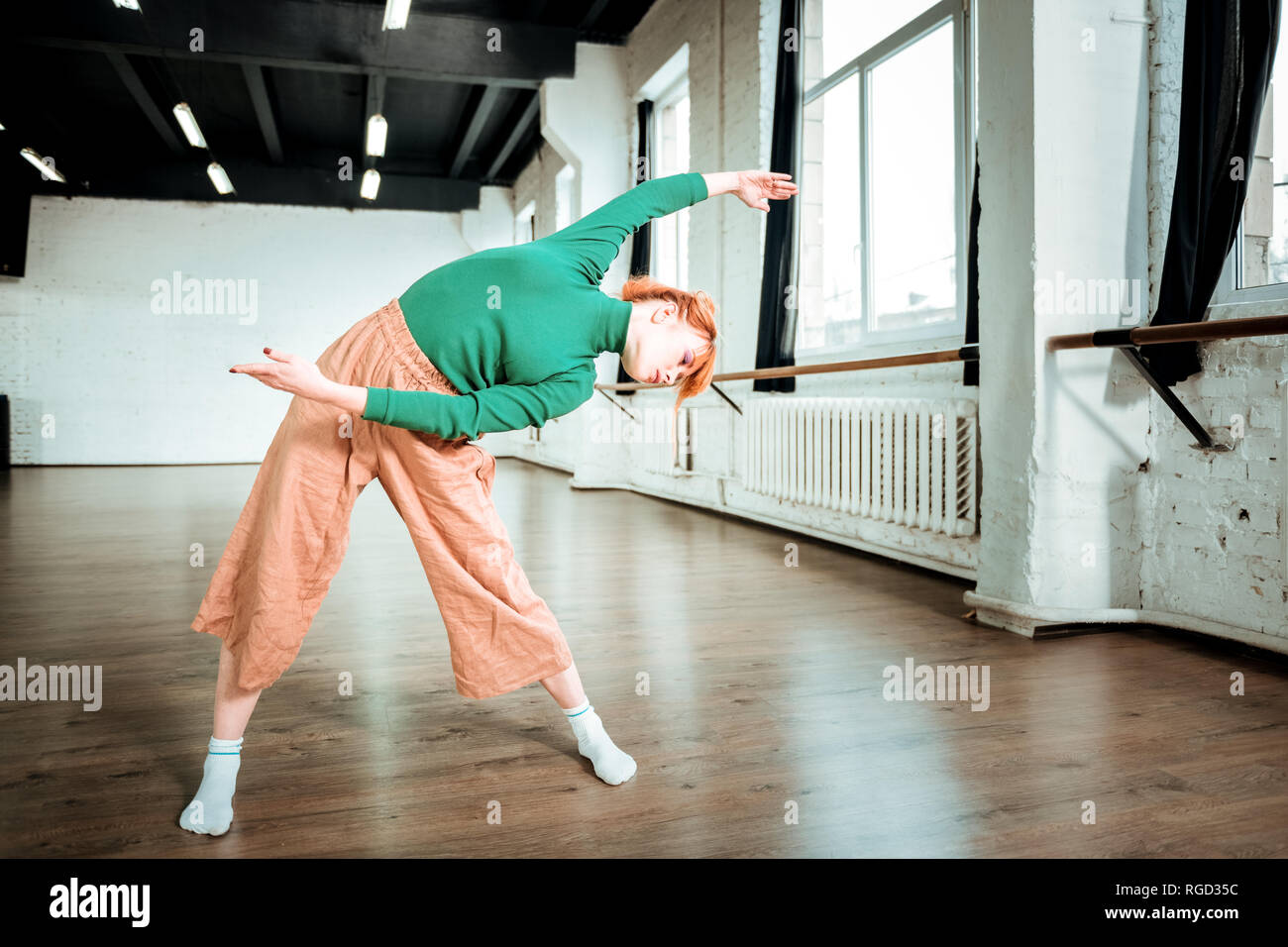 Pleasant-looking red haired yoga instructor in a turtleneck doing ...