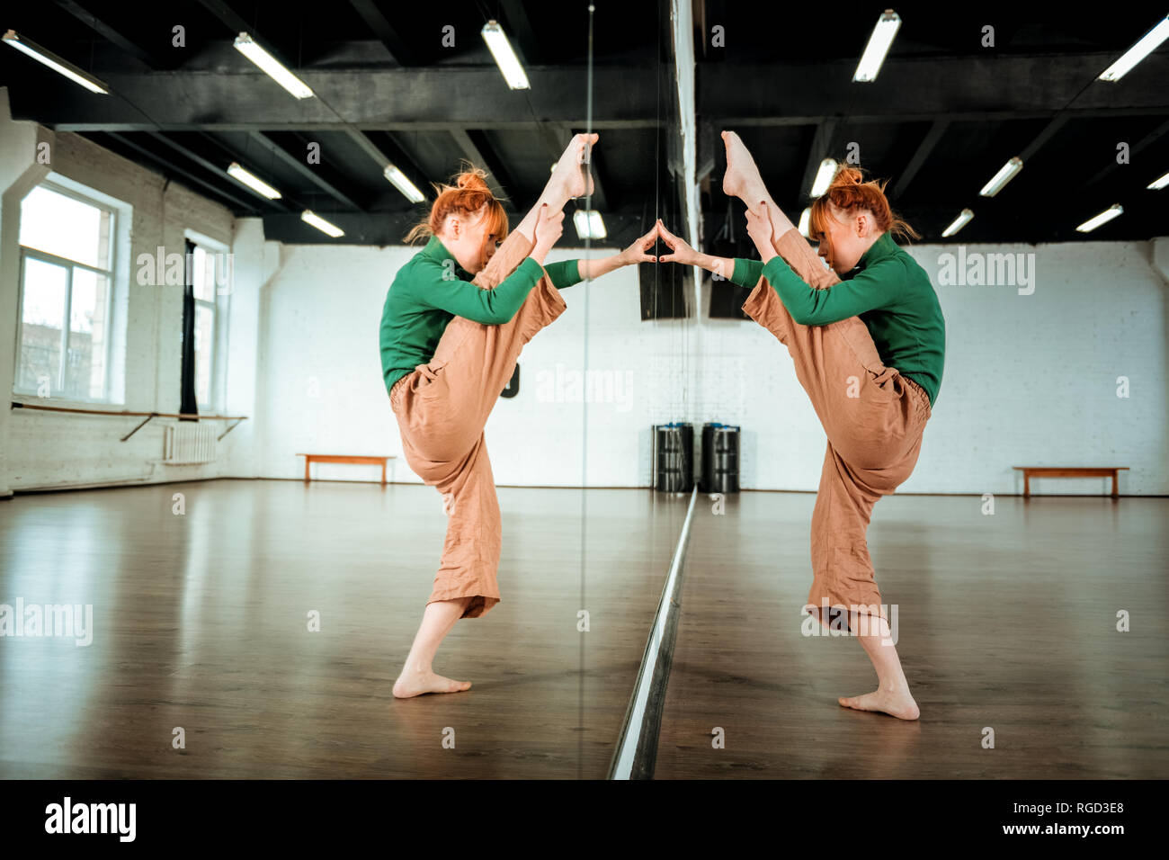 Cute red-haired dance teacher in a green turtleneck doing leg-split ...