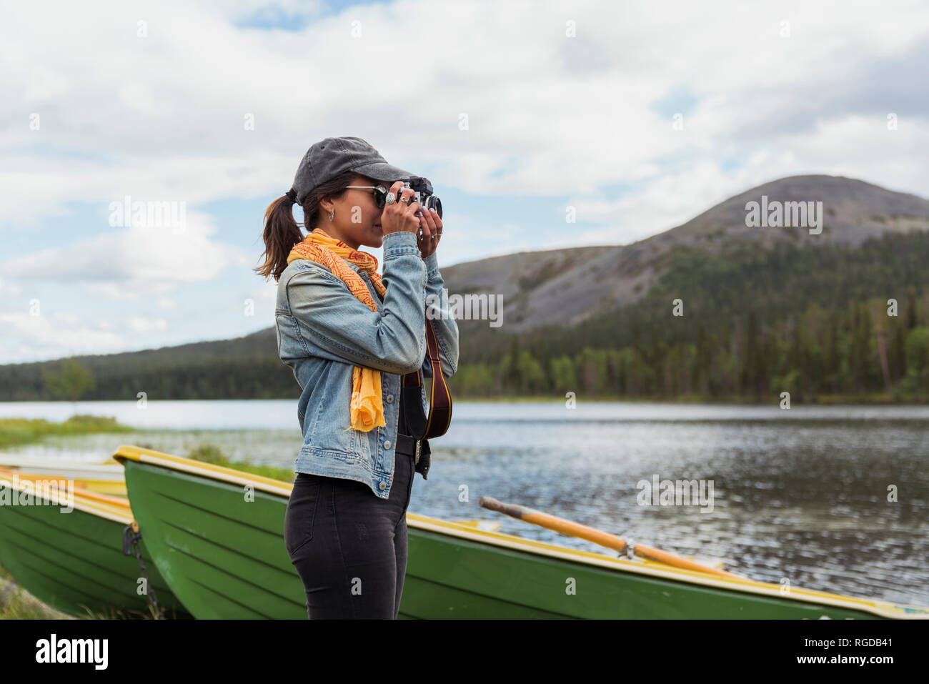 Finland, Lapland, woman taking picture with a camera at the lakeside ...