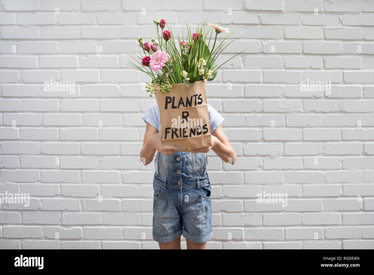 Girl hiding behind paper bag with flowers Stock Photo - Alamy