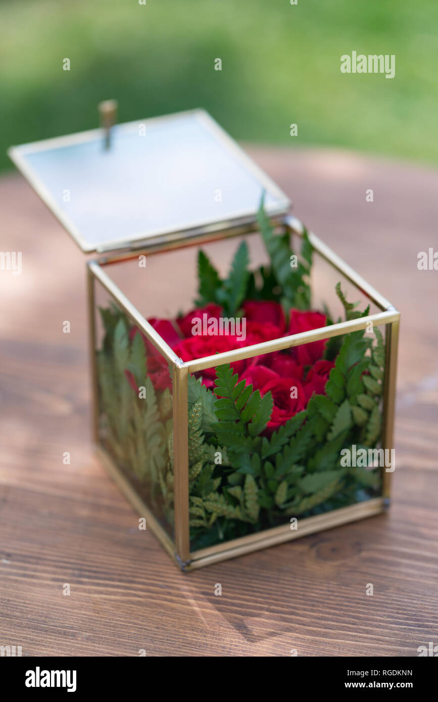 glass box with red flowers and greenery for wedding rings, close up ...