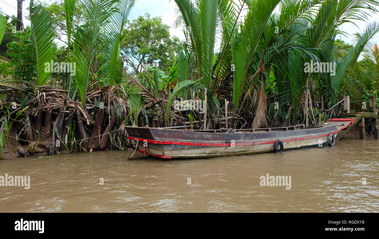 Wooden long fishing boat in a muddy river, along the riverbank with ...