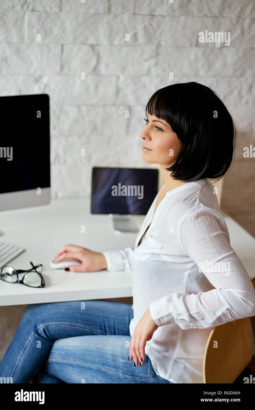 Attractive businesswoman working on computer at her workstation with ...