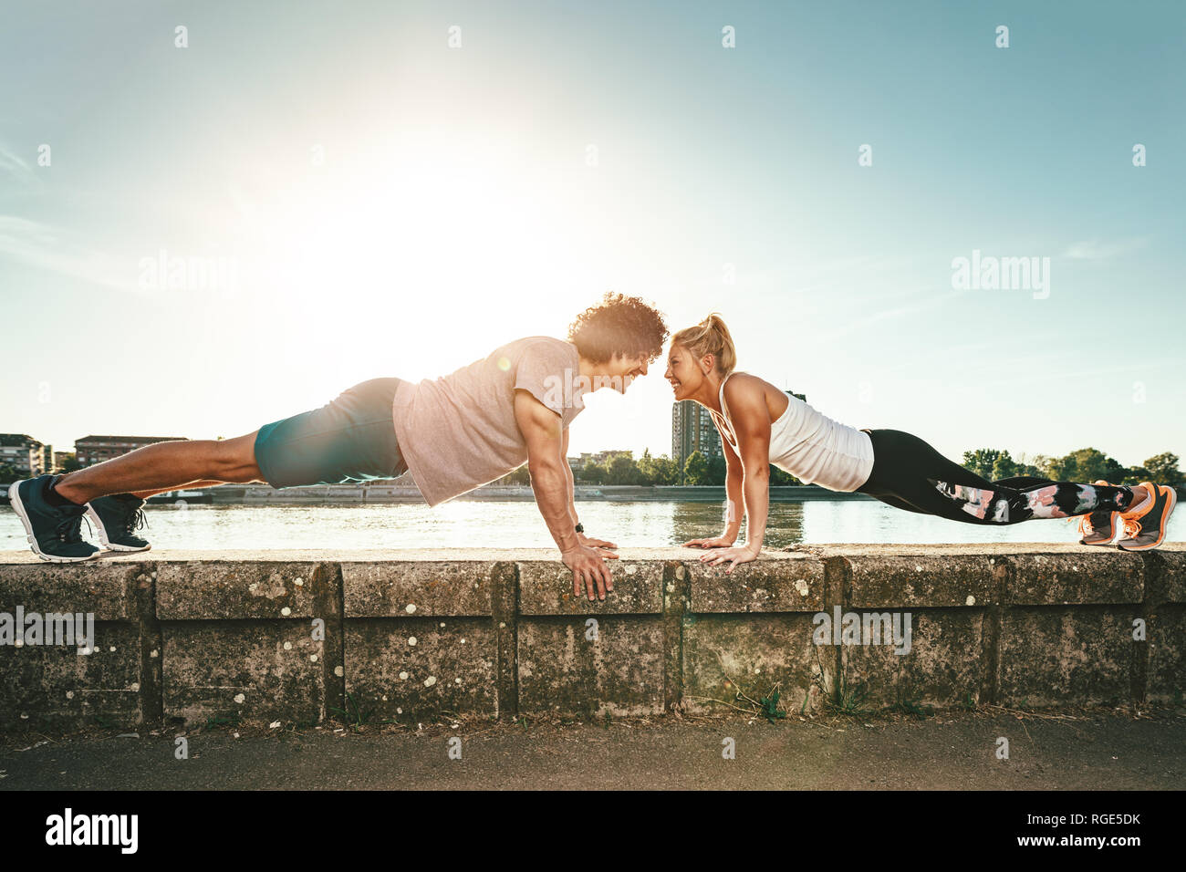 Young happy smiling couple is training outdoors doing push-ups during ...
