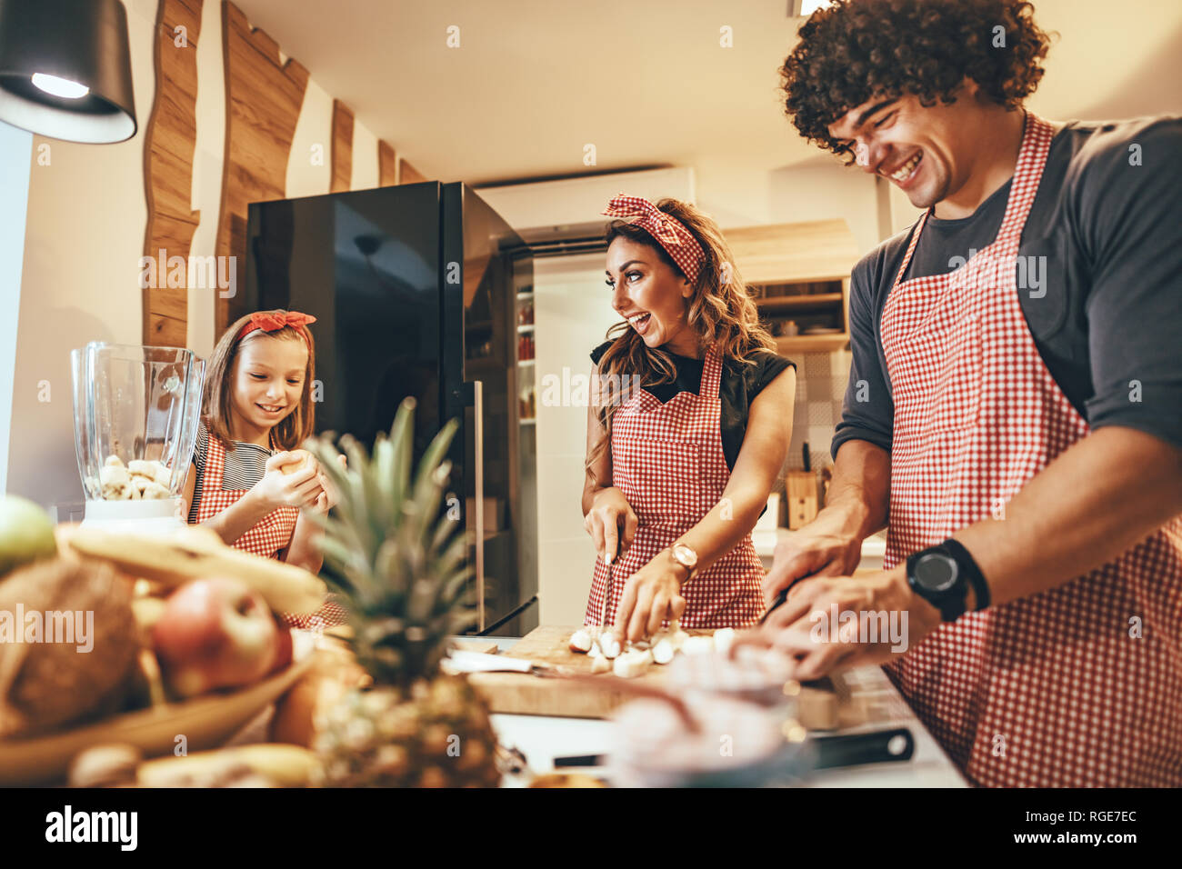 Happy parents and their daughter cooking together in the kitchen while ...