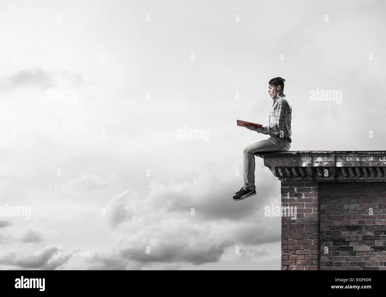 Man on roof edge reading book and cloudscape at background Stock Photo ...