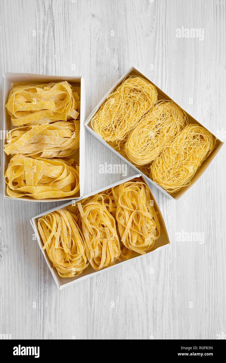 Set of various uncooked pasta in boxes on white wooden surface, top ...