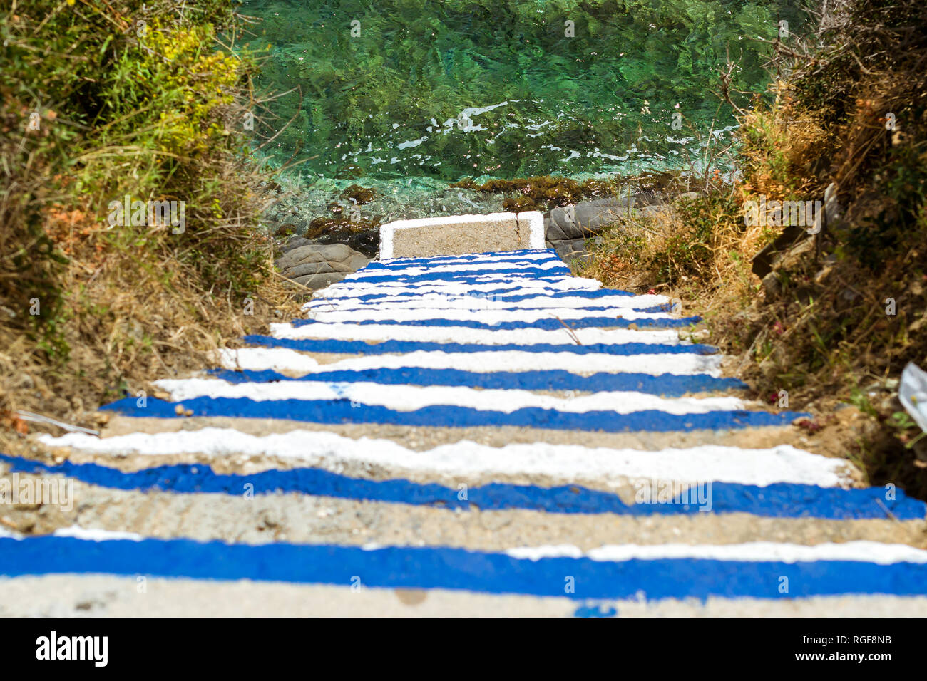 Concrete stairs down to ocean. Steps painted in colors of Greek flag ...