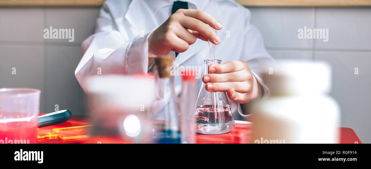 Little boy scientist extracting liquid from flask against of chalkboard ...