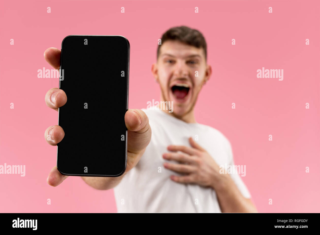 Young handsome man showing smartphone screen over pink background with ...