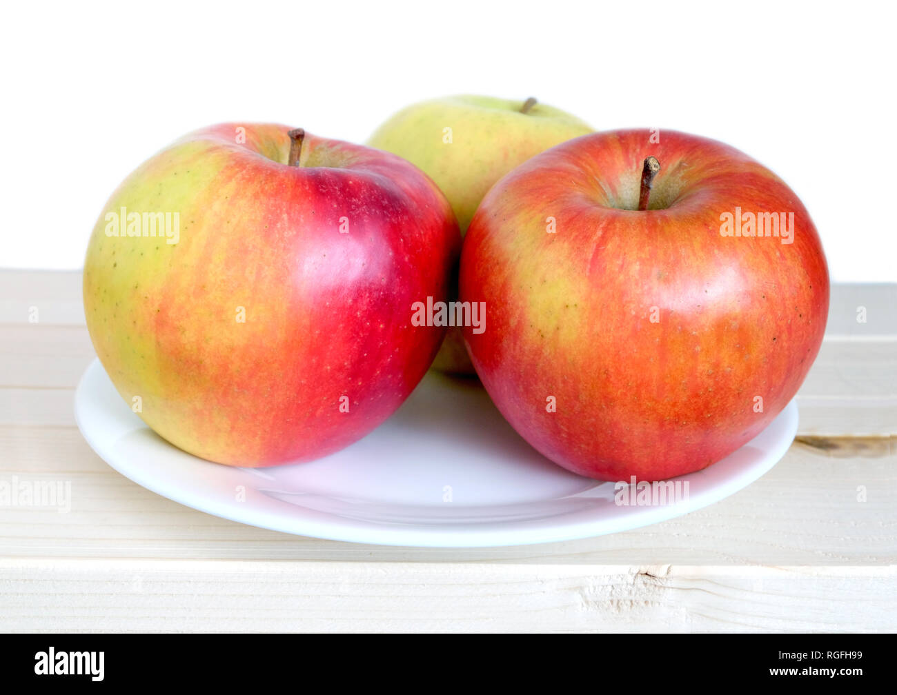 Three big ripe apples on white plate in wooden shelf on white ...