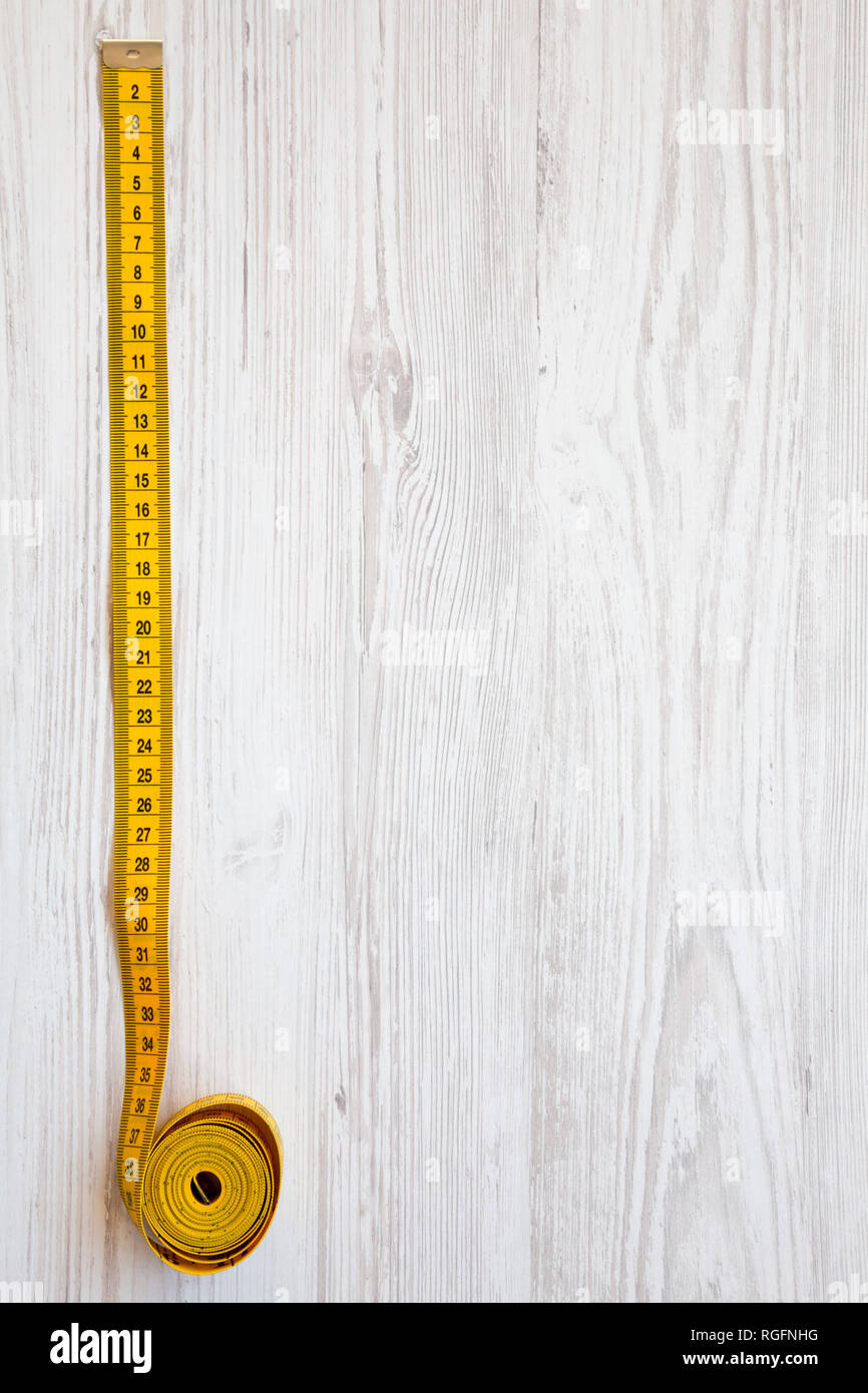 Yellow measuring tape on white wooden surface, overhead view. From ...