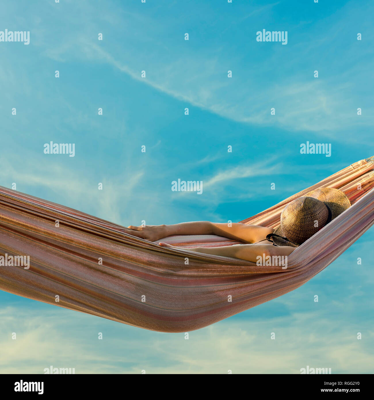 Woman relaxing in a hammock against a hazy blue sky with her straw ...