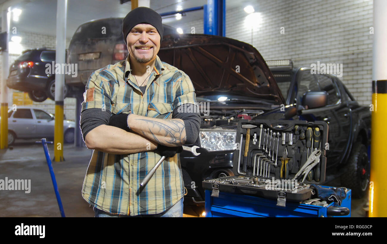 Car service. Brutal mechanic man standing by the car and smiling Stock ...