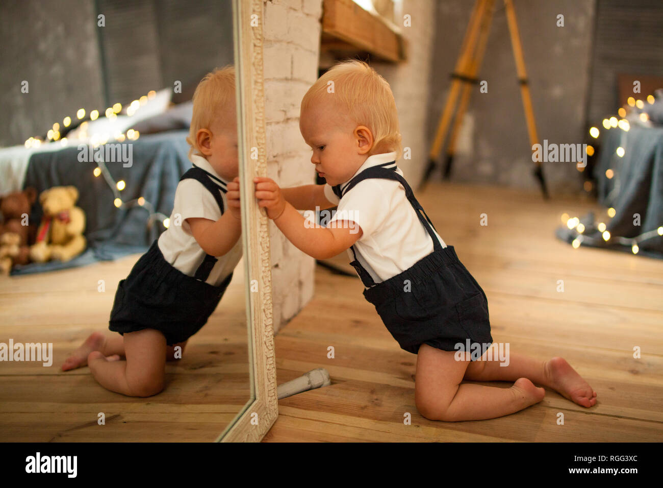 Baby boy plays near the mirror against background of garland of glowing ...