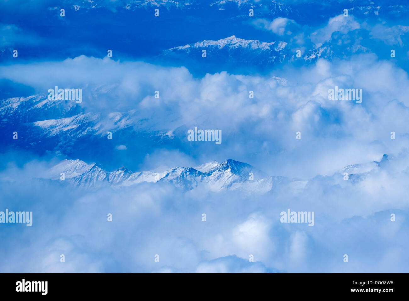 Aerial view of snow covered mountains peeking trough the clouds as seen ...