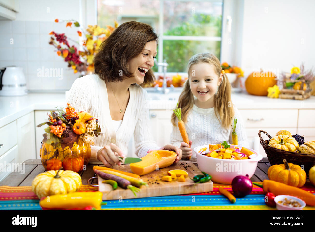 Mother and daughter cutting pumpkin, onion and carrot, cooking soup for ...