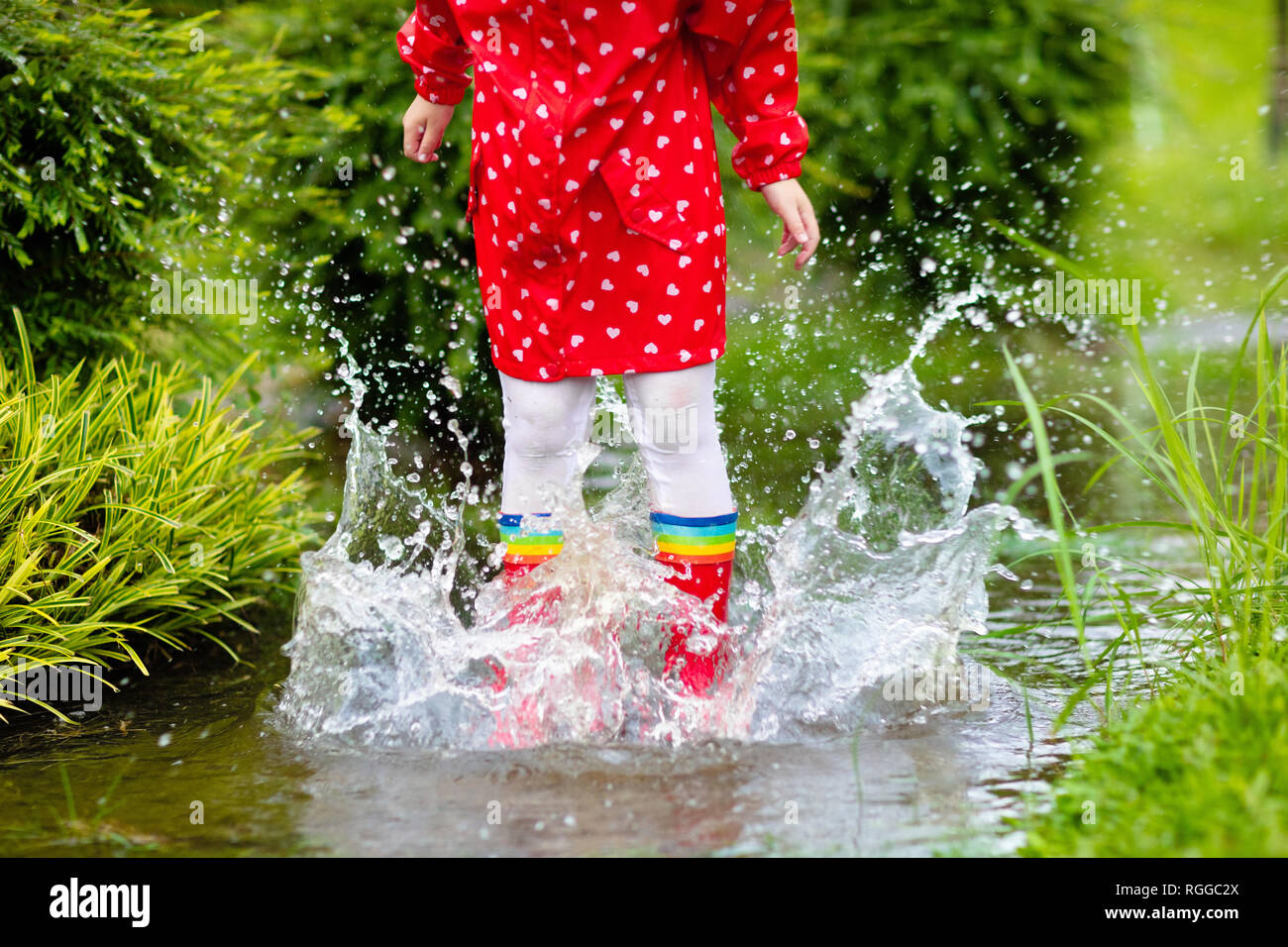 Kid playing in the rain in autumn park. Child jumping in muddy puddle ...