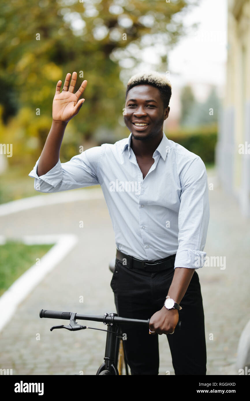 Portrait of handsome young man waving hello near bike in the street ...