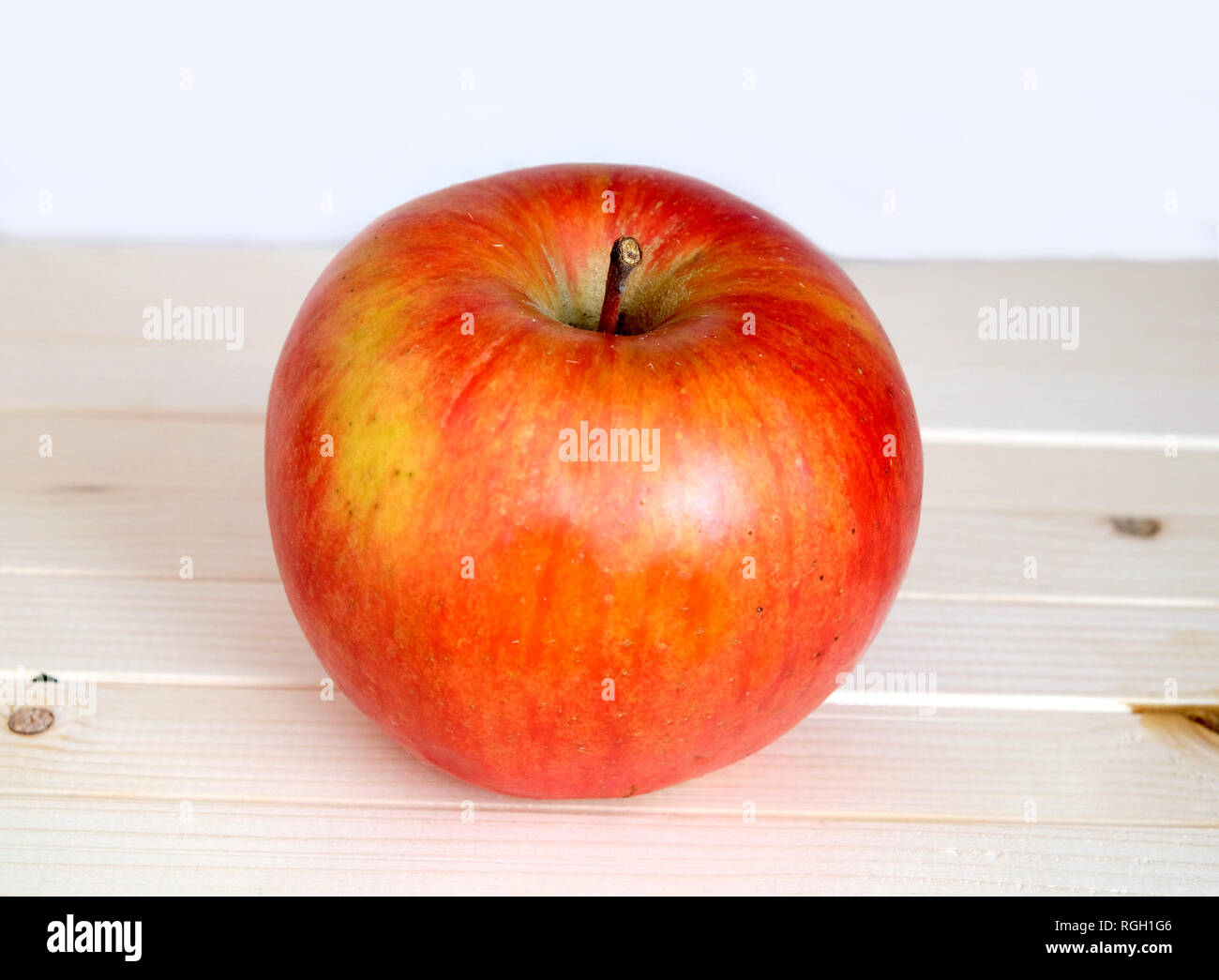Big ripe red apple in beige wooden shelf on white background front view ...
